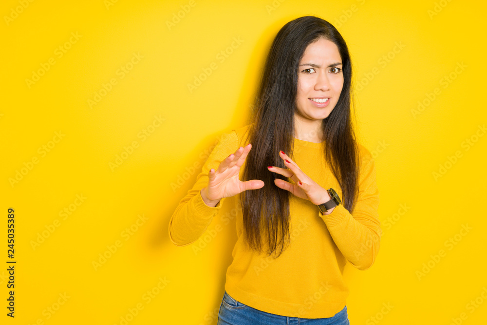 Beautiful brunette woman over yellow isolated background disgusted ...