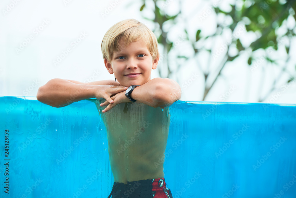 Portrait of smiling boy resting in pool with transparent walls and blue ...