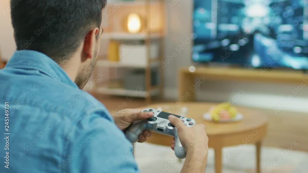 In the Living Room Man Sitting on a Couch Holds Controller Playing in a ...