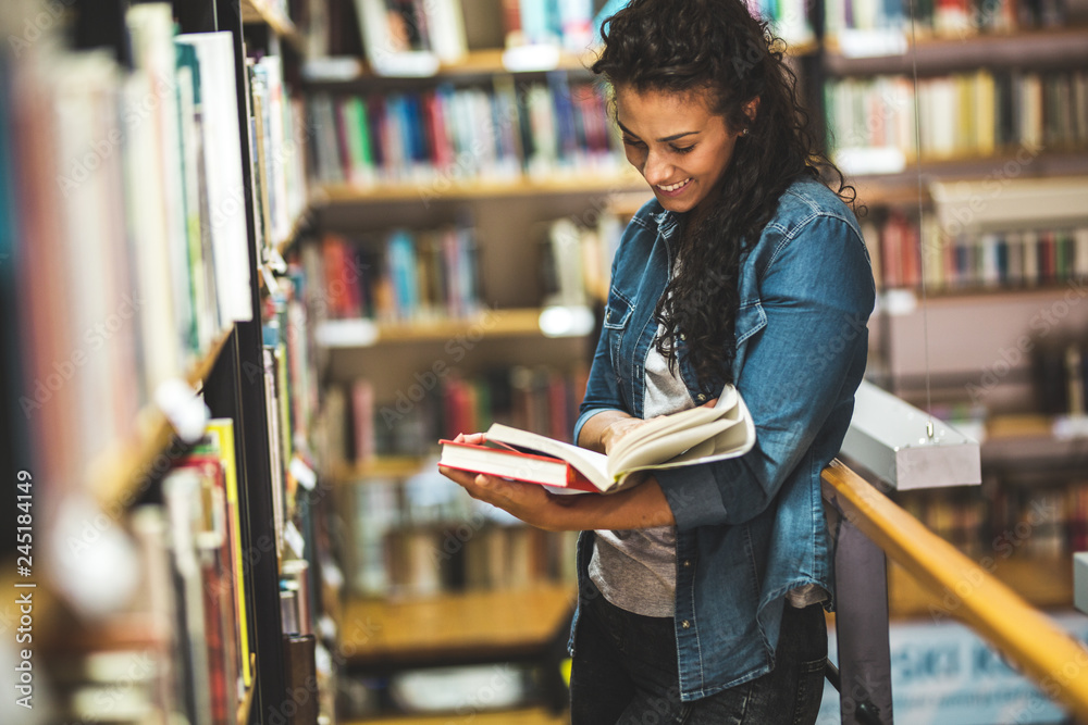 Young female student read and learns by the book shelf at the library ...