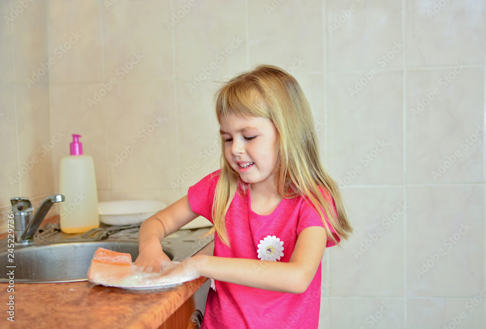 Little girl washes the dishes. Beautiful little girl washes a plate in ...