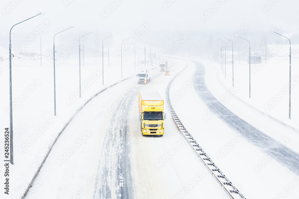 Traffic on the highway in a snow blizzard. Cars on a snowy asphalt road ...