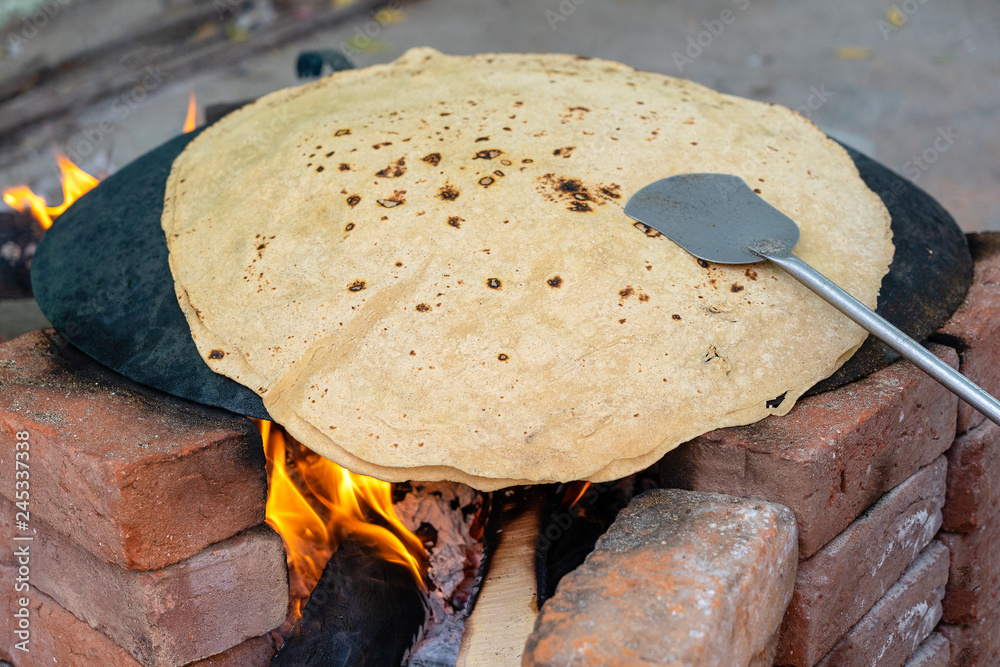 Woman cooking traditional indian bread, big chapati cooking on open ...