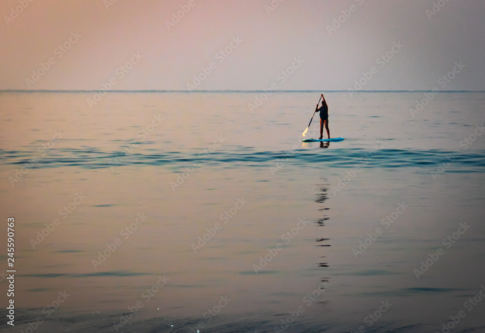 Stand up paddle boarding on a quiet sea with warm summer sunrise colors ...