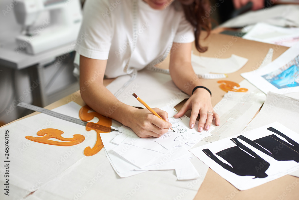 Young smiling female designer drawing pencil sketches of clothing ...