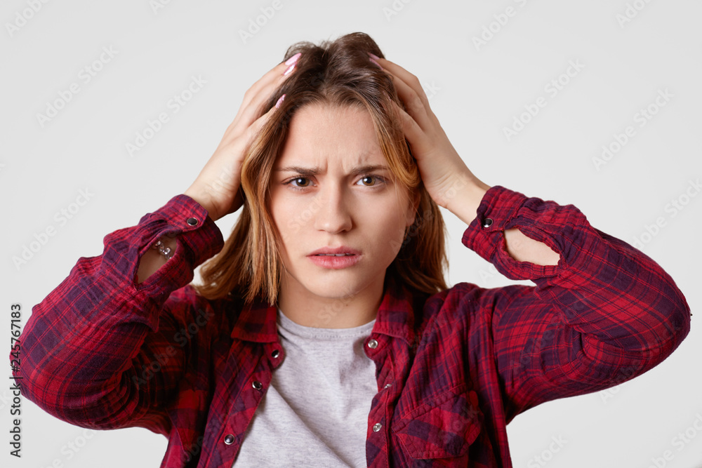 Perplexed tired overwhelmed young woman keeps hands on head, frowns ...