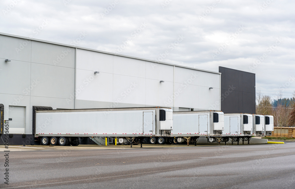 Long refrigerator semi trailers stand in row in warehouse docks with ...