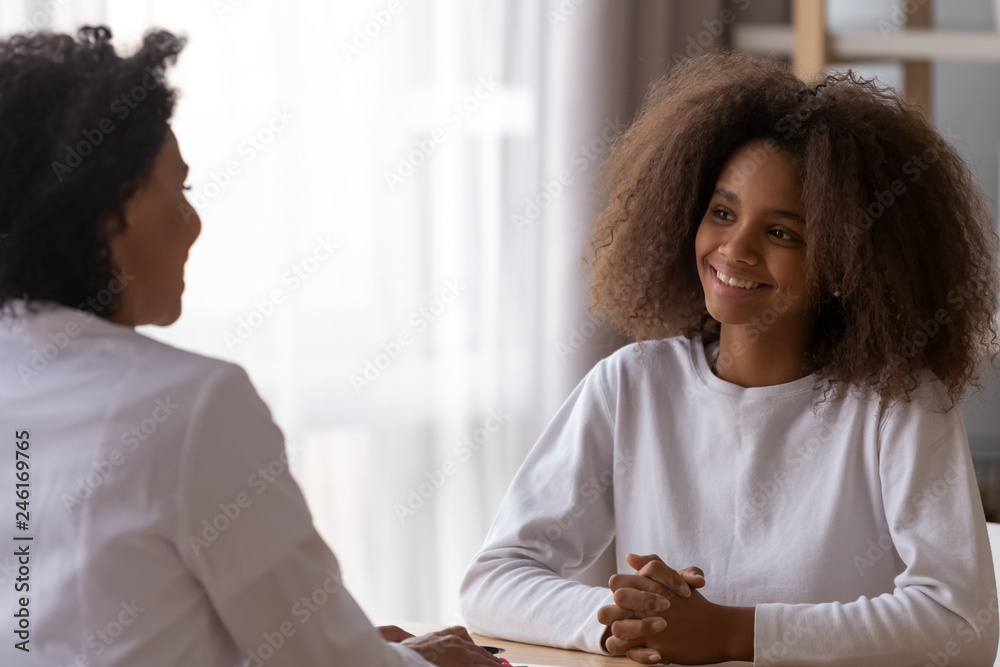 Smiling African American teenage girl sit at table talking with female ...