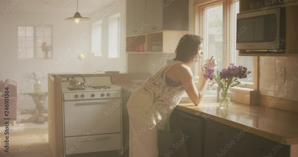 A woman leans on her counter in her modern kitchen. She is looking out ...