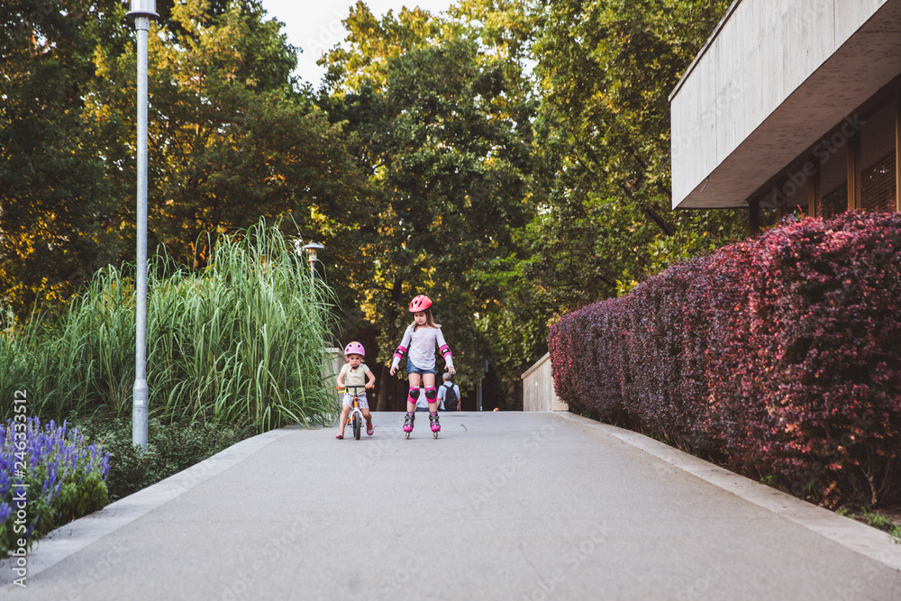 Two little girls rides on rollers and runbike in summer park. Children ...