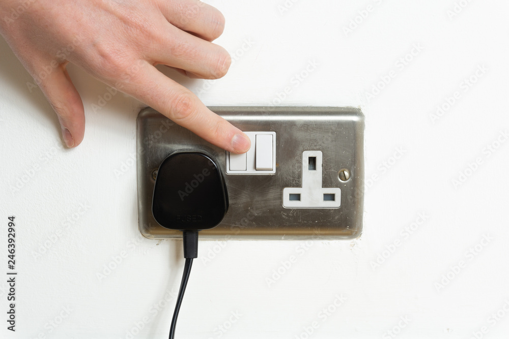Stainless steel UK plug socket on white wall with hand switching on ...