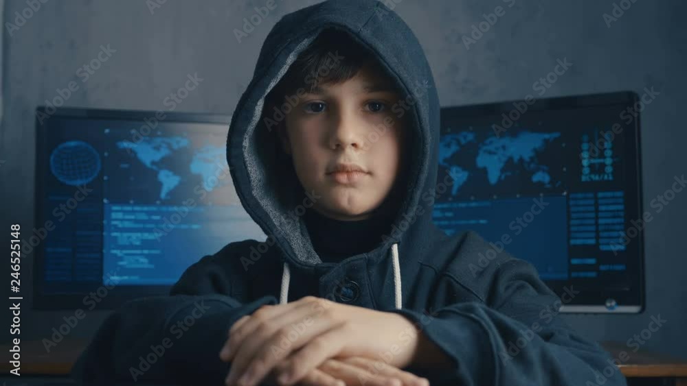 Boy wonder Hacker in hood at data center filled with display screens ...