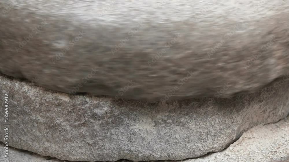 Close-up footage of medieval hand-driven millstone grinding wheat. The ...