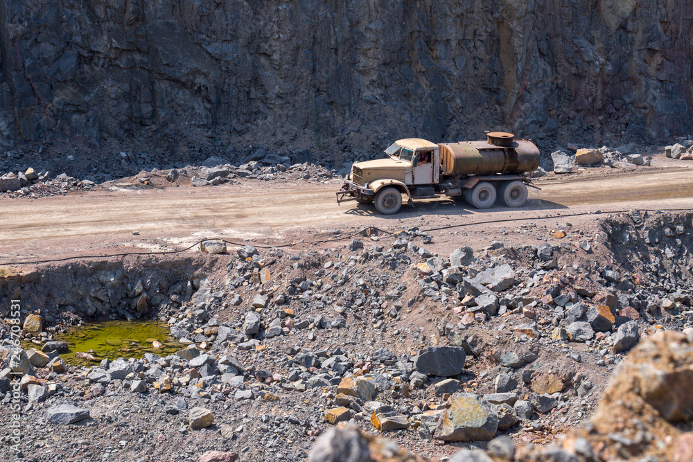 The tank truck wets water the surface of the road in a quarry open pit ...