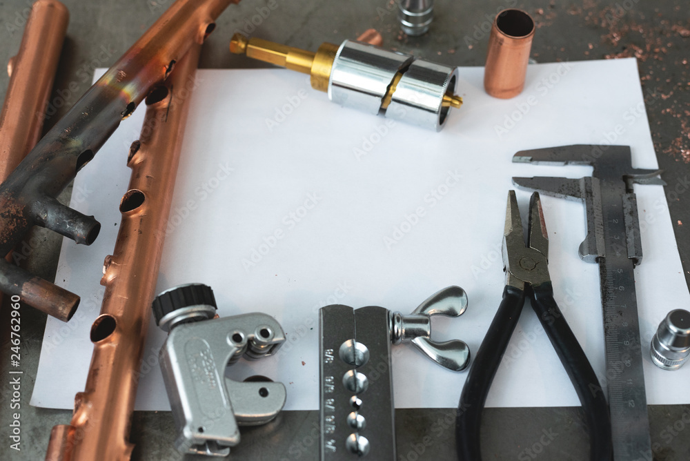 Brass pipes, pipe cutter, calipers, pliers and a blank layout drafts of ...