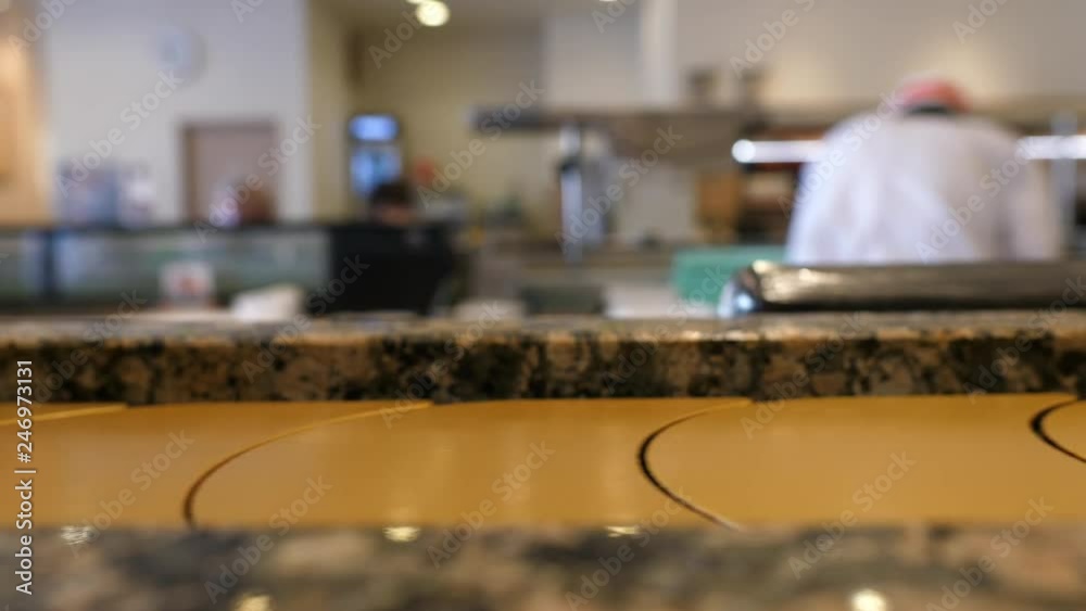 Chef prepares sushi as other dishes go around on the conveyor belt in a ...