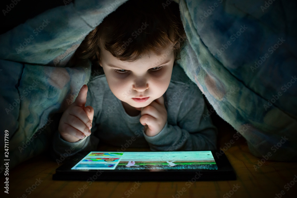 Little girl watching her tablet in the bed. Illuminated child face from ...