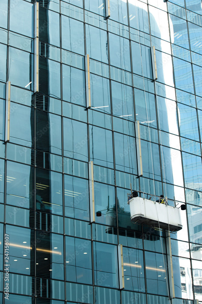 Workers crane cradle clean windows glass of high building under sun day ...