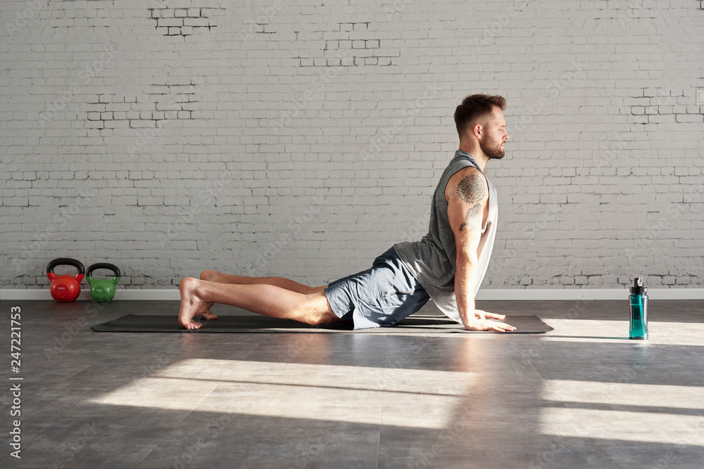 Tattooed muscular man exercising yoga asana plank in sunny sport club ...