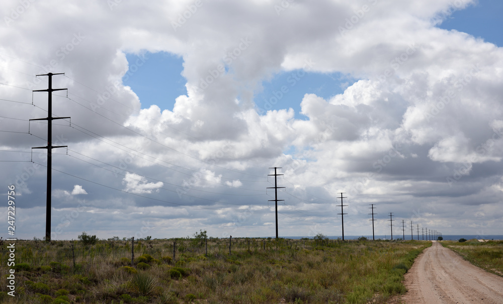 Long row of utility poles and high voltage power lines, empty road and ...