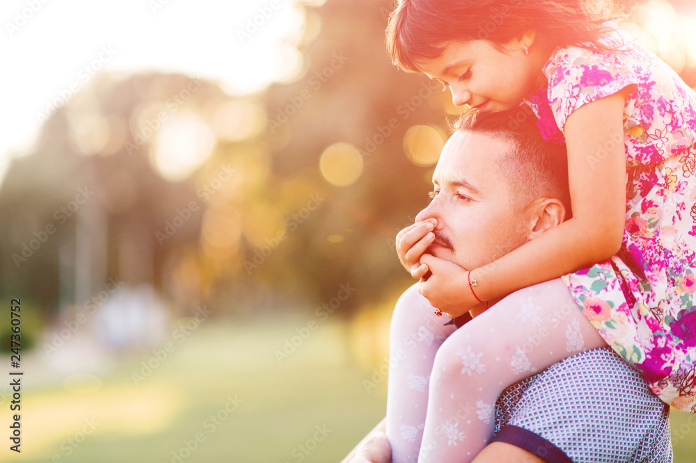 Dad carrying his daughter on shoulders in summer park at sunset. Father have fun with his little ...