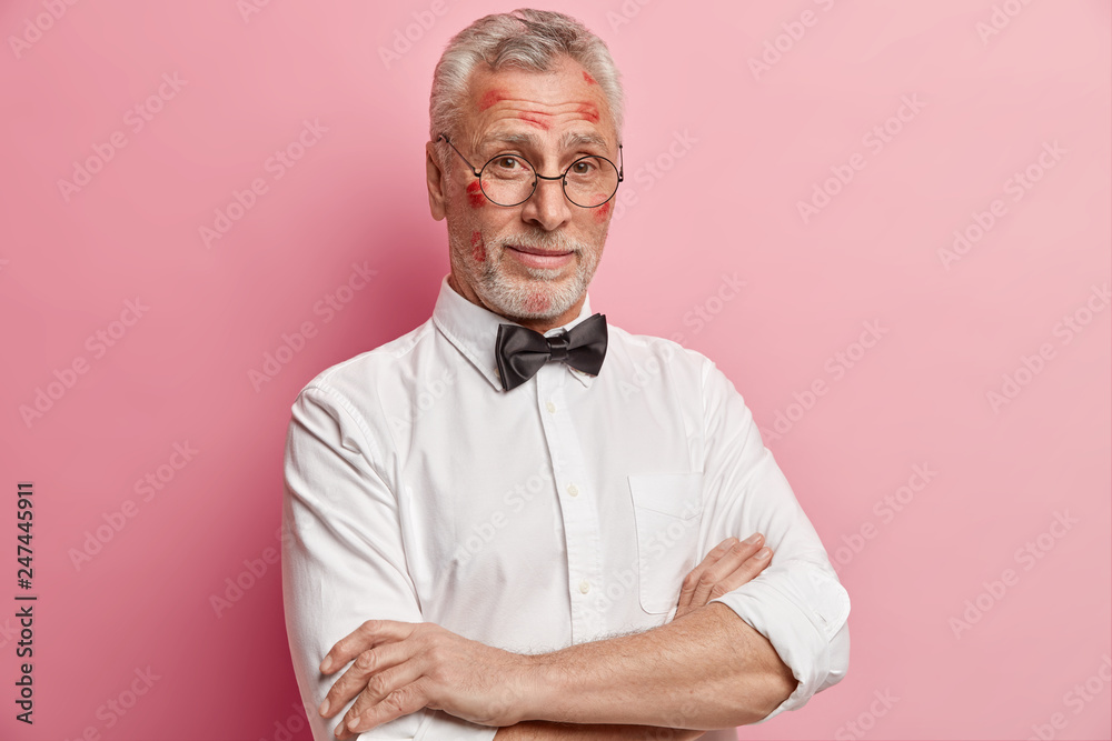 Attractive grey haired man with thick stubble, keeps hands crossed ...