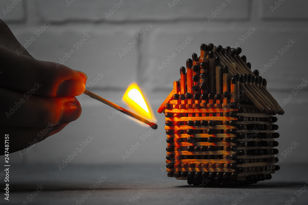 hand with a burning match sets fire to the house model of matches, risk ...