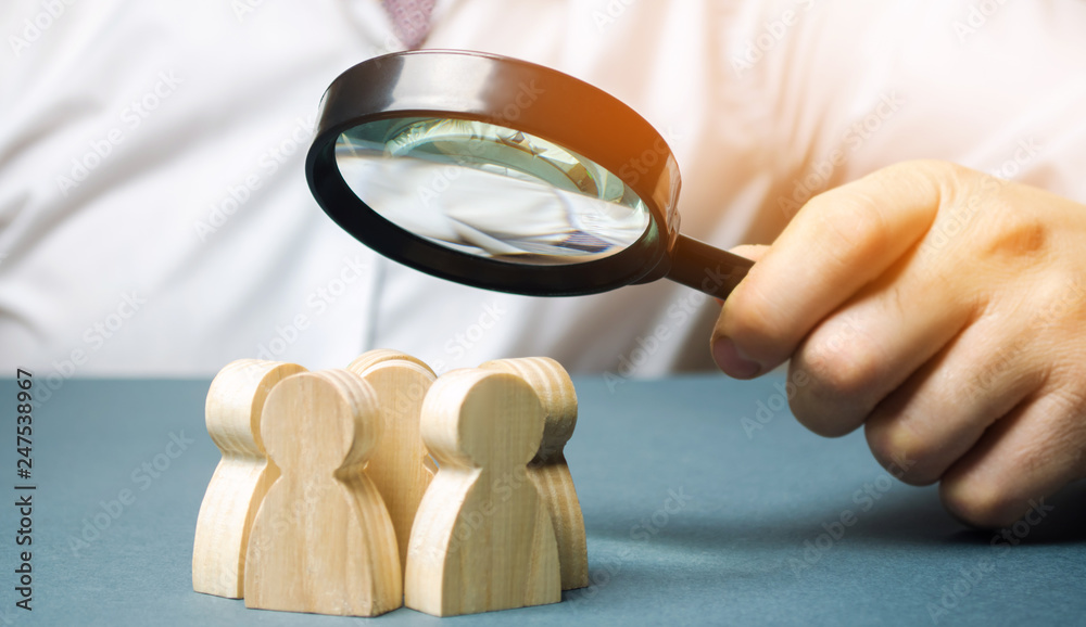 Business leader holding a magnifying glass over a team of workers. The ...