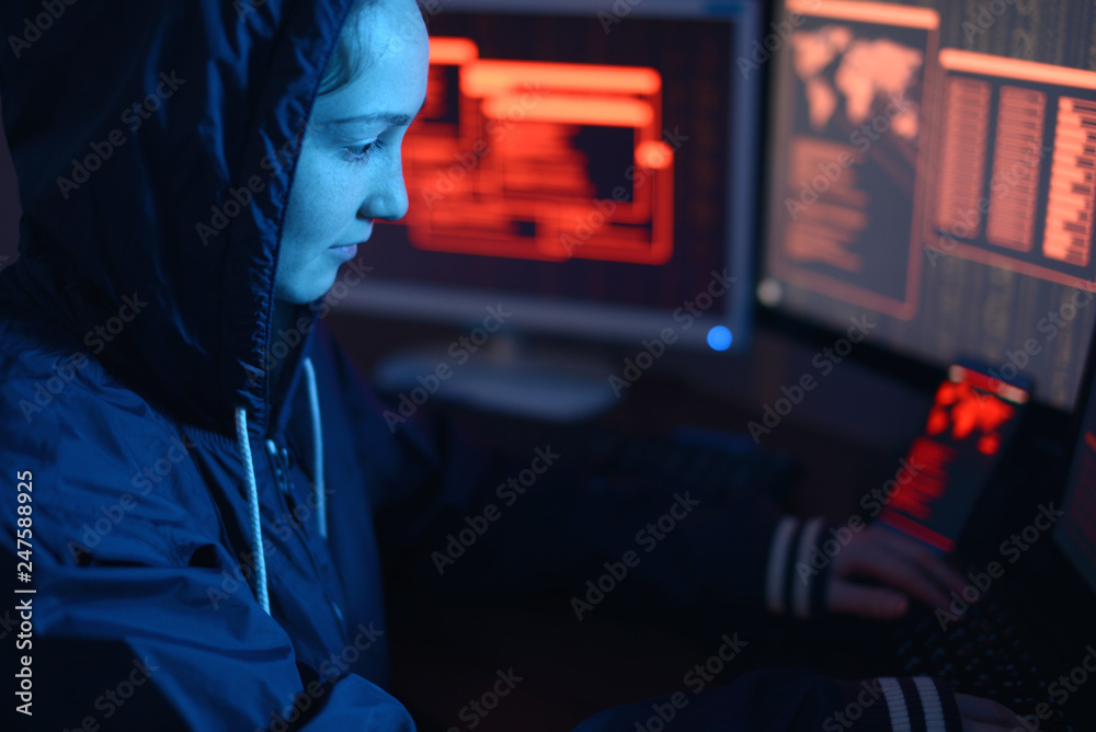 Girl hacker in a hood typing program code while committing a cybercrime hacking a system on the ...