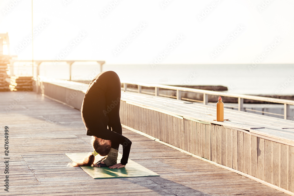 Young woman practicing yoga, standing forward bend pose, doing head to ...