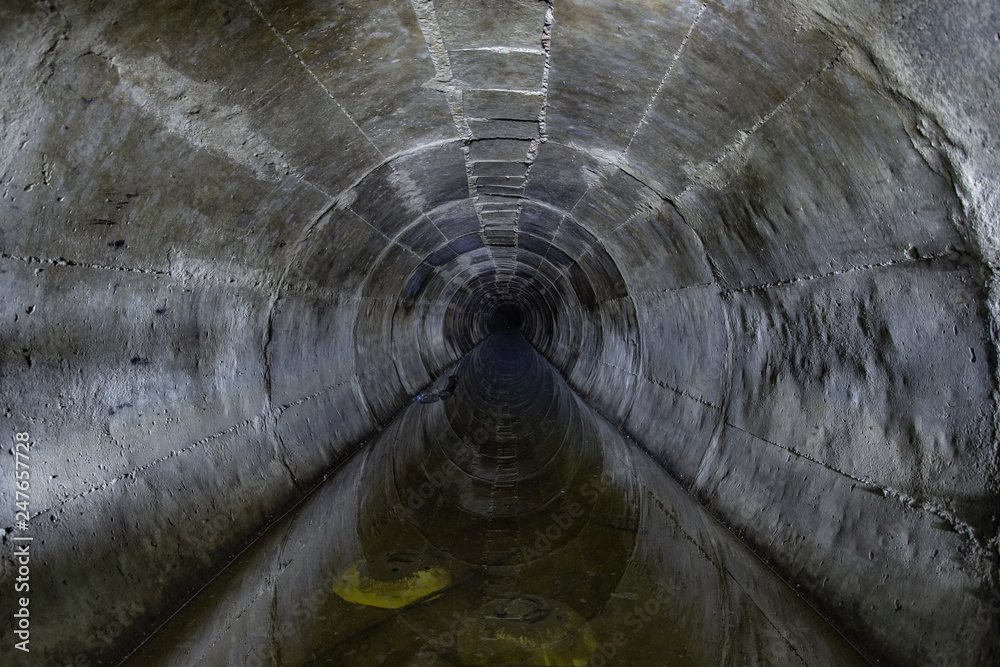 Flooded round underground drainage sewer tunnel reflecting in dirty ...