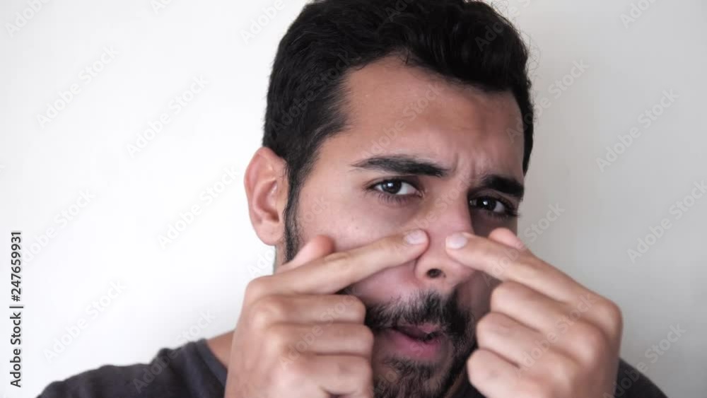 Attractive man popping and squeezing his nose pimples looking at the ...