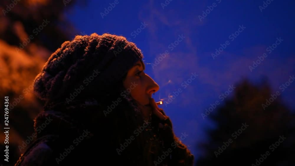 Girl smoking outside in winter, at night. Close up on a thoughtful ...