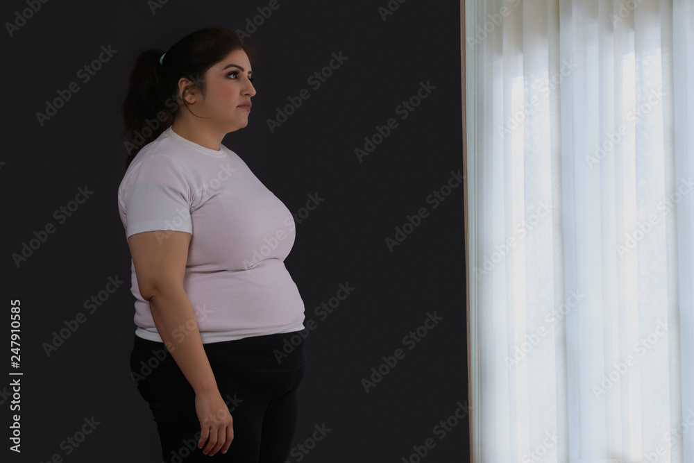 Sad obese woman looks while standing by the window Stock Photo | Adobe ...