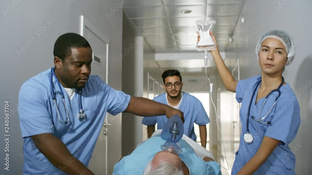 Dolly shot of multi-ethnic group of ER nurses in scrubs administering ...