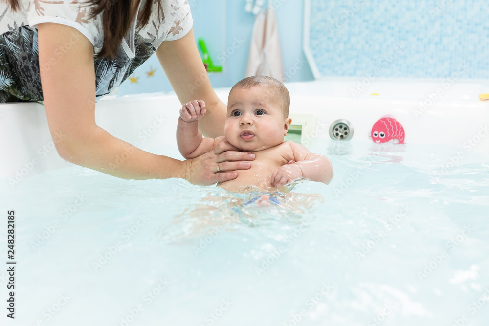 Newborn baby swimming in the bath or bathtub. Mother help him swim. Mom ...