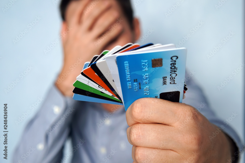 Confused man looking at many credit cards uncertain which one to choose ...