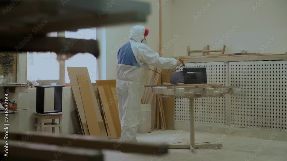Factory worker spray painting furniture parts at an assembly line ...