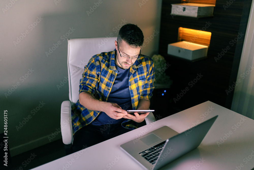 Young employee using tablet while sitting in the office late at night ...