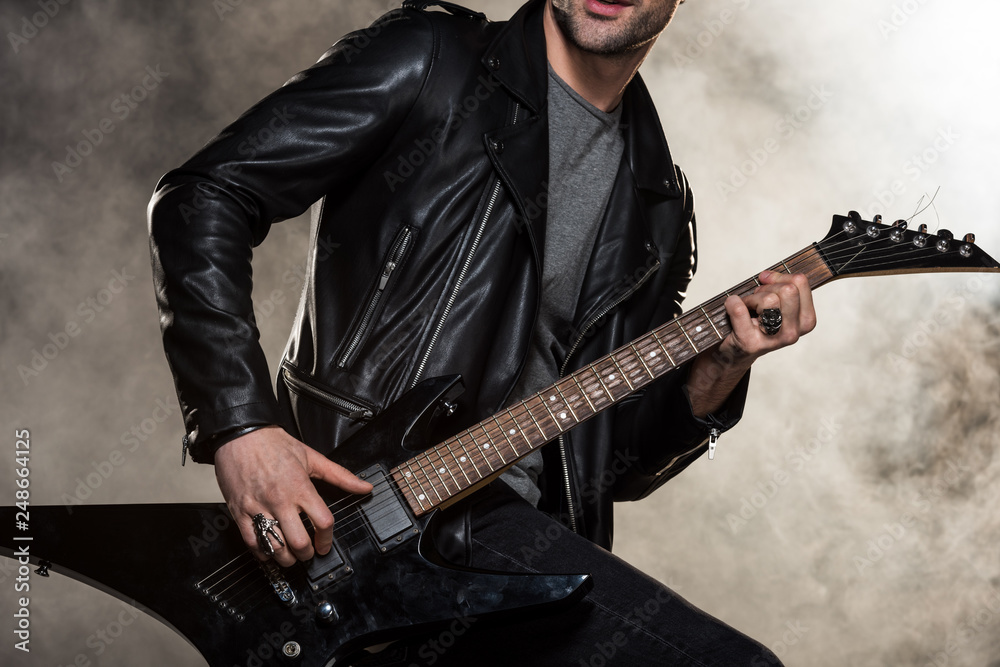 cropped view of rocker in leather jacket playing electric guitar on ...