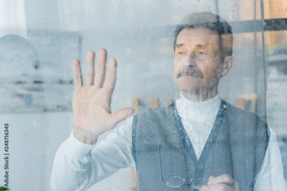 sad senior man waving hand while standing near window Stock Photo ...