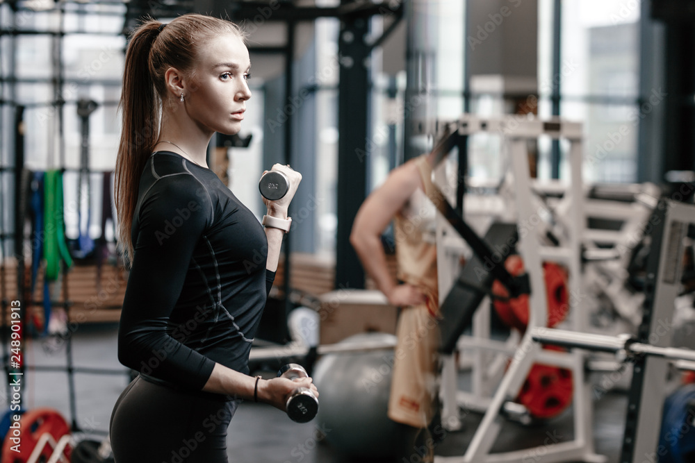 Slender young girl dressed in a black sportswear is doing exercises ...
