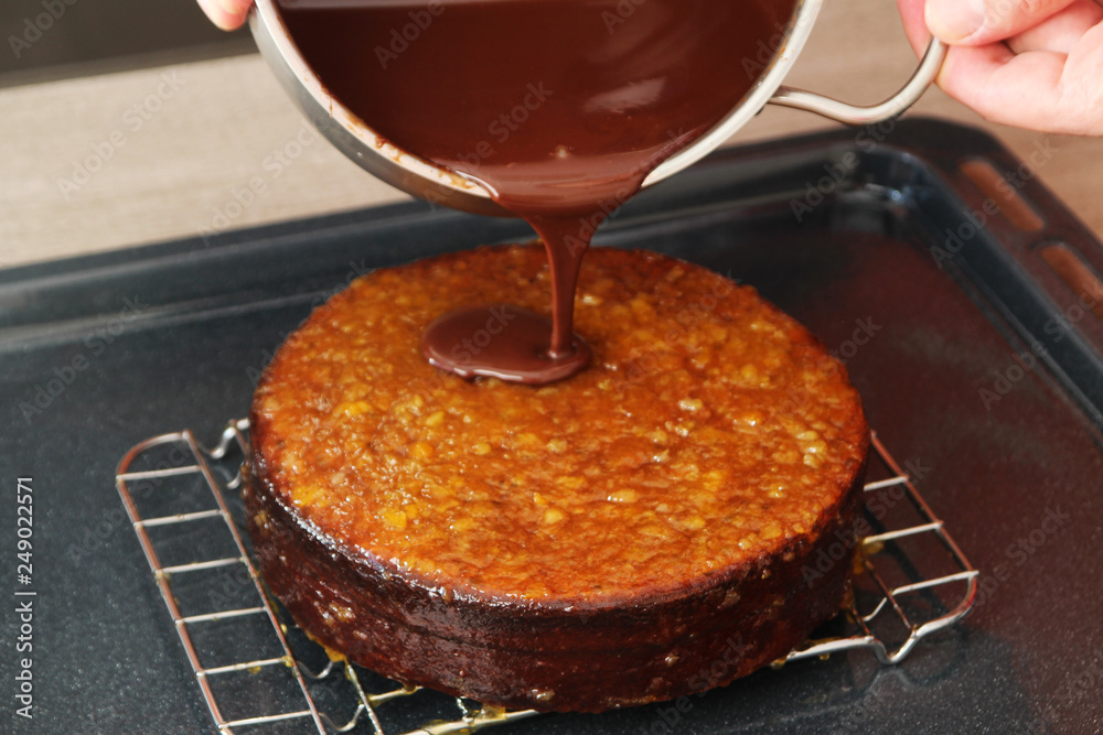 Liquid chocolate is spilling on cake to make icing of traditional cake ...
