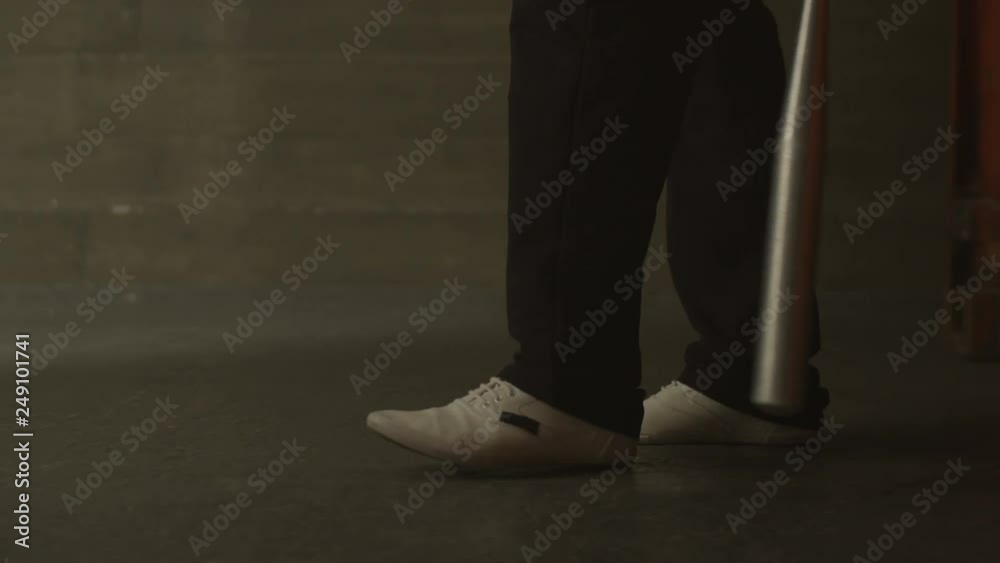 Low section of aggressive thug with sport bat walking along dark street ...