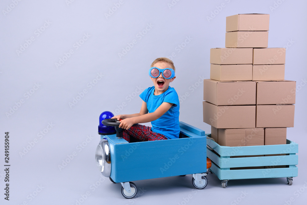 Smiling boy driving blue, fanny car and wagon with small boxes.Happy ...