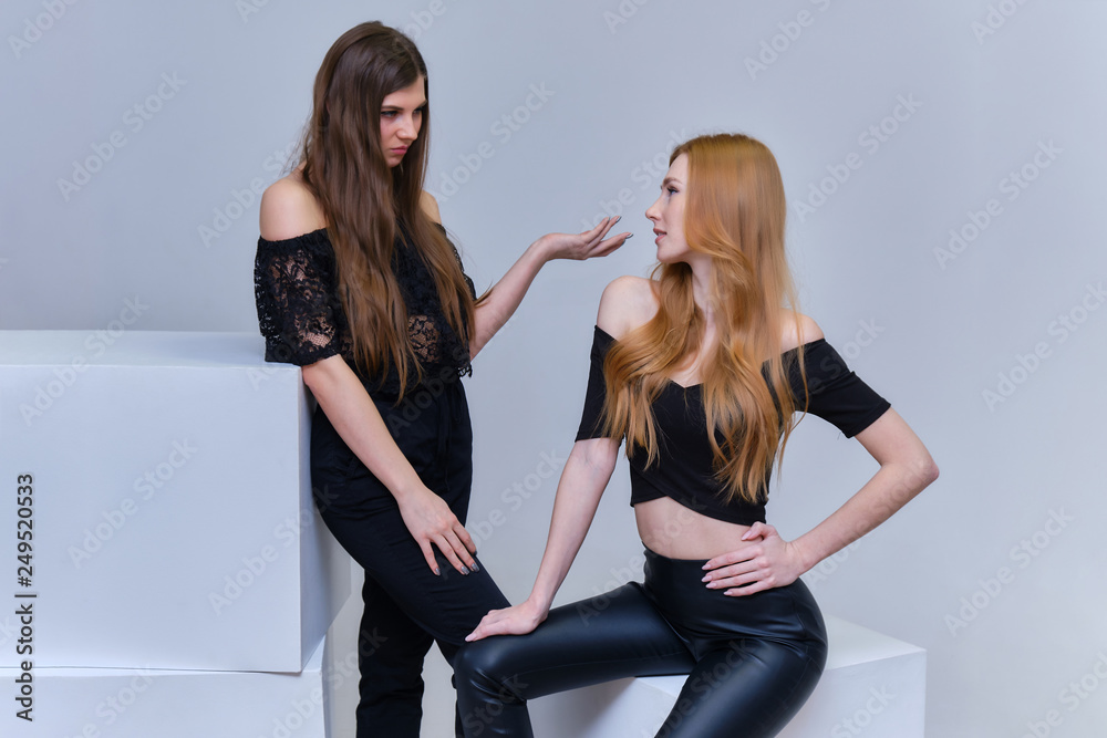 Concept portrait of two cute beautiful girls talking on a gray ...