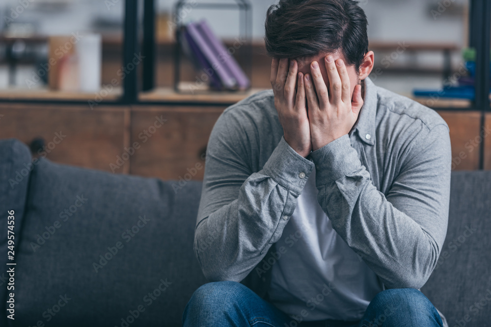 man sitting on couch, crying and and covering face with hands at home ...