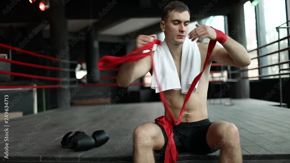 Bare-chested boxer man unwrapping his boxing red bandages and stretches ...