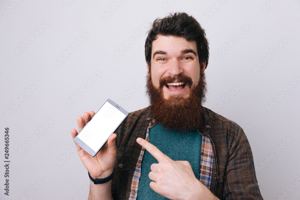 Shot of hansome guy isolated on grey background, presenting smart phone ...