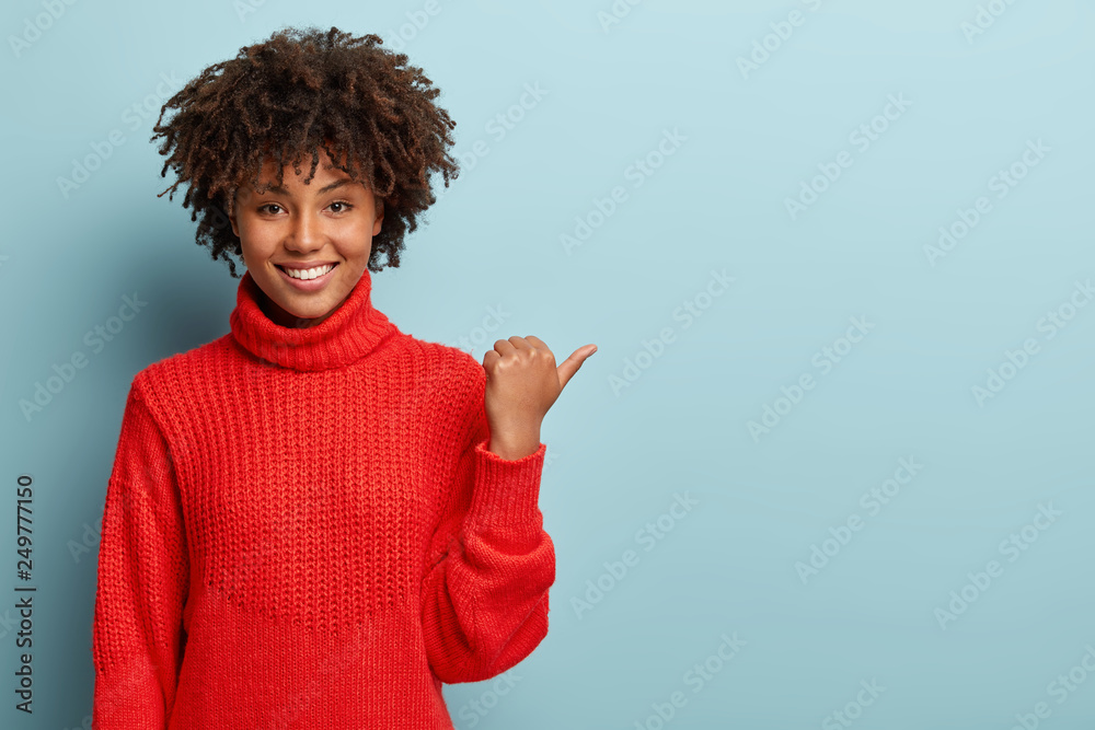 Smiling black woman with Afro hairstyle, wears red jumper, points with ...